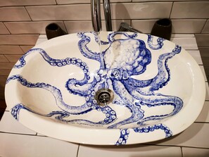 Uma pia de banheiro com design de polvo, uma torneira e dois dosadores de sabonete.