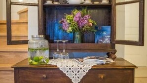 Um armário de madeira com portas abertas exibindo uma chaleira, xícaras e um vaso com flores.