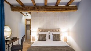 Quarto com uma cama grande, duas luminárias de cabeceira, teto de madeira, uma escrivaninha com cadeira e um espelho.