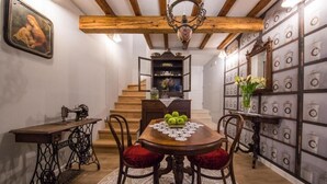 Uma sala de jantar com uma mesa de madeira, cadeiras estofadas em vermelho, toalha de renda e uma escada que leva a outro espaço.