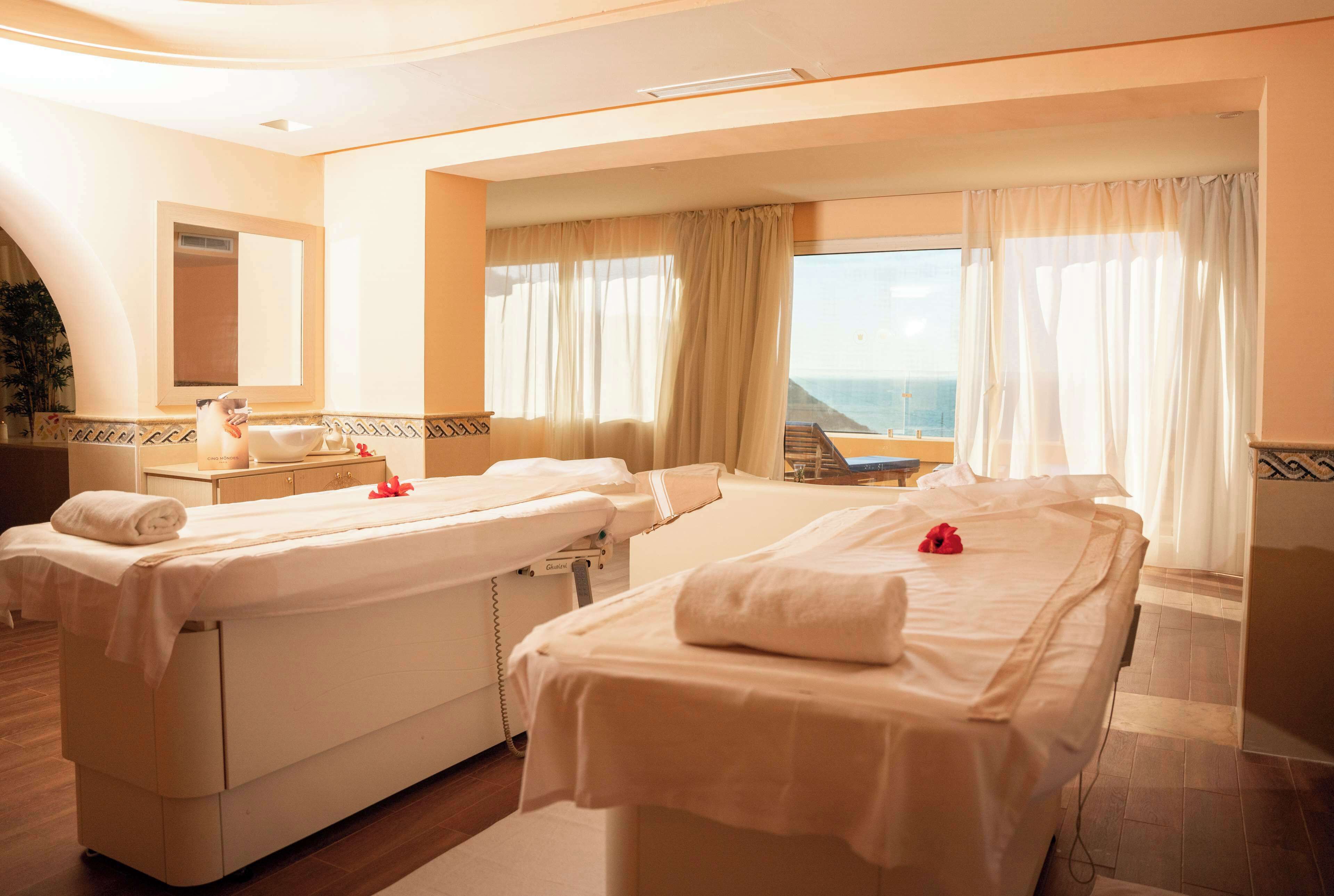 Quarto de hotel com duas camas, uma janela grande com vista, um espelho e uma mesa pequena com luminária.