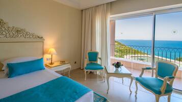 Quarto de hotel com cama, uma cadeira, uma mesa e varanda com vista para o mar.