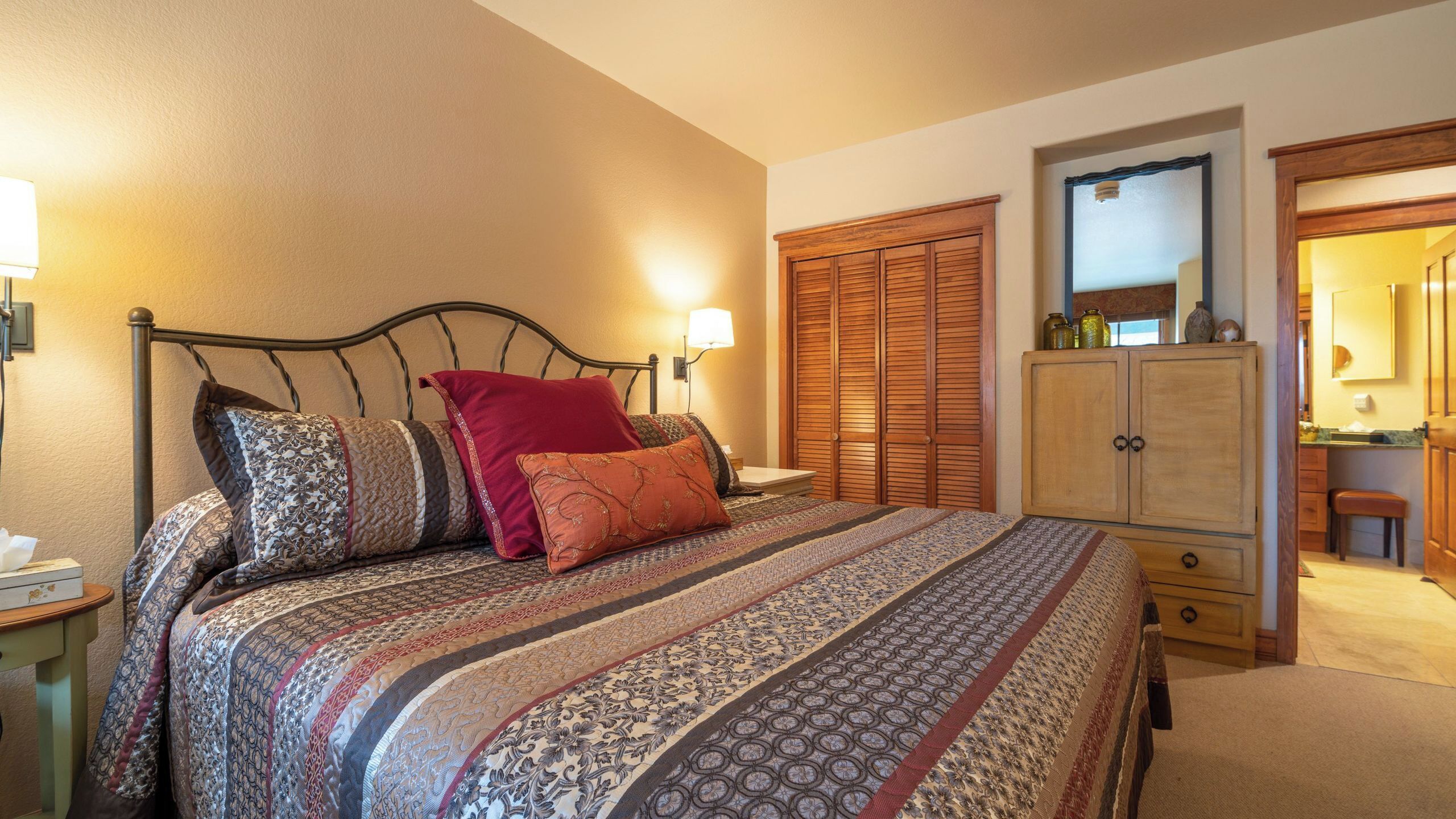 Quarto com cama, mesas de cabeceira, guarda-roupa e espelho.