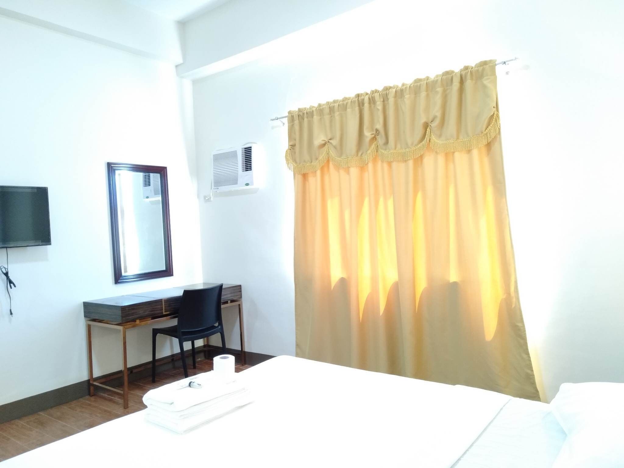 Quarto de hotel com uma cama, uma escrivaninha com cadeira, uma televisão e um ar condicionado.