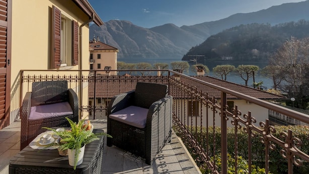Varanda com móveis de vime e mesa posta para dois, com vista para um lago e montanhas.