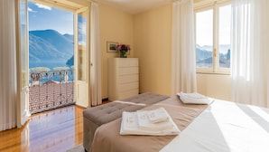 Quarto de hotel com uma cama, penteadeira e vista para montanhas através de grandes janelas.