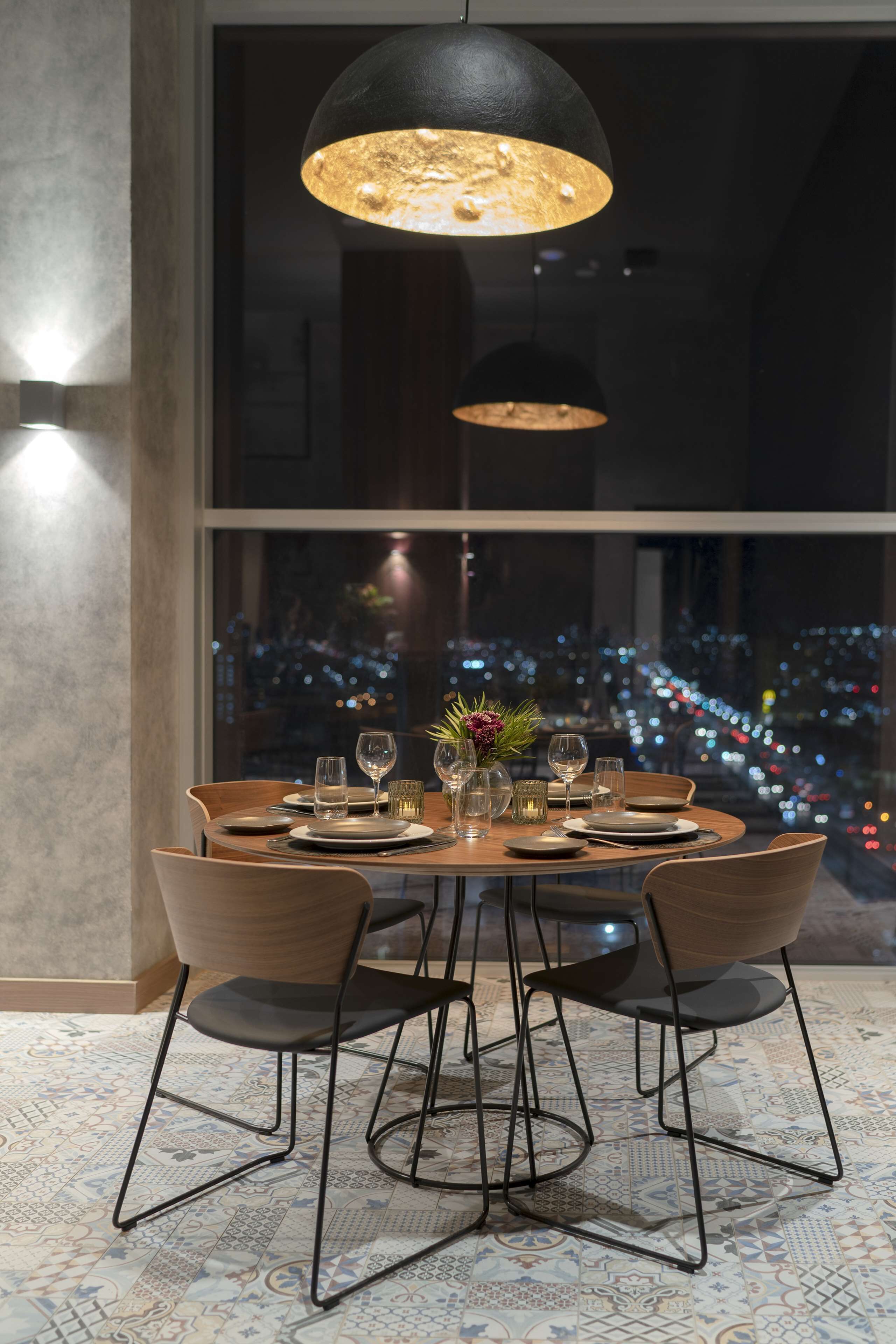 Uma área de refeições com uma mesa redonda para seis pessoas, cadeiras pretas e uma grande janela com vista noturna da cidade.