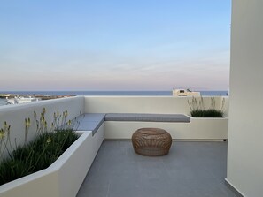 Terraço no telhado com área de estar, uma cadeira de vime e vista para o mar.