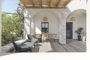 Um pátio externo com mesa e cadeiras, cercado por paredes e arcos brancos.
