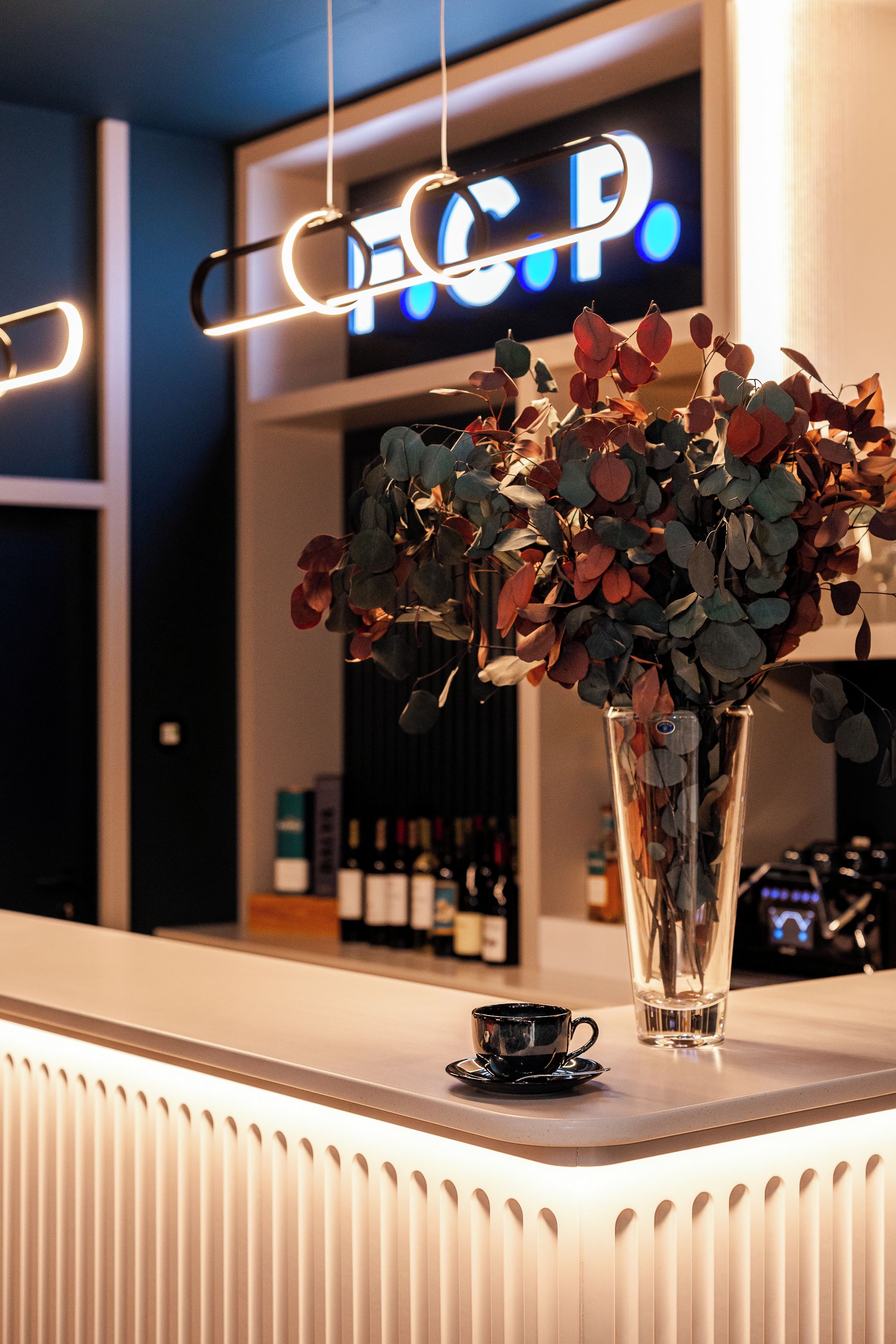 Uma área de recepção com um vaso de folhagem, uma xícara e uma placa luminosa.