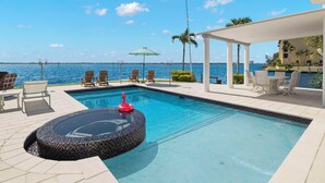 Uma área de piscina com espreguiçadeiras, uma banheira de hidromassagem e vista para o mar.