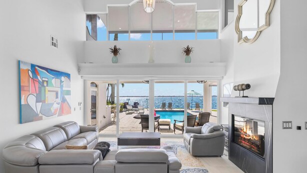 Uma sala de estar ampla com sofá seccional cinza, lareira e vista para a piscina e oceano.
