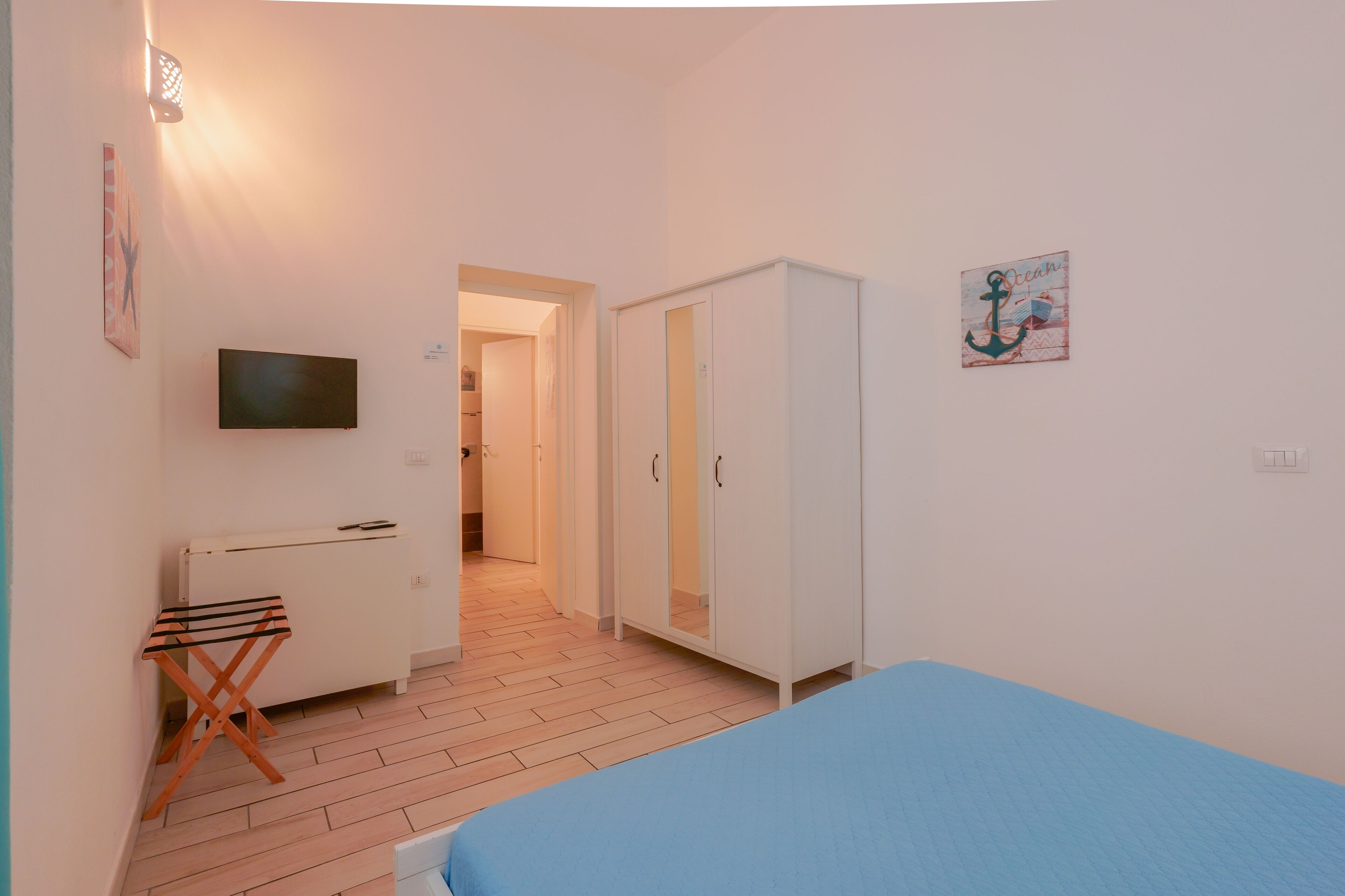 Quarto com cama, guarda-roupa, televisão e uma pequena mesa.