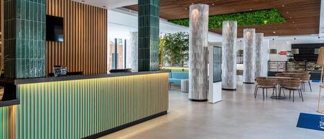 Uma área de recepção moderna com um balcão de atendimento em padrão verde e amarelo, painéis de madeira vertical e uma parede verde com planta.