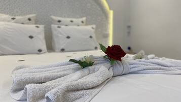 Cama bem arrumada com lençóis brancos e uma rosa vermelha.