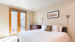 Quarto com uma cama grande, mesa de cabeceira, cômoda e porta de vidro deslizante para uma varanda.