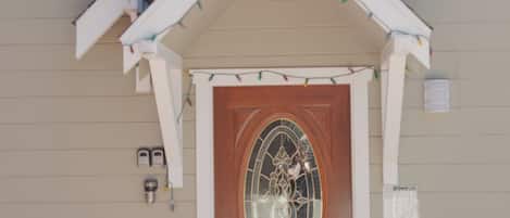 Uma casa com porta de madeira, janela com detalhe em vidro decorativo e caixa de correio na parede.