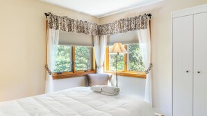 Um quarto com uma cama, duas janelas com cortinas, uma luminária e um guarda-roupa.