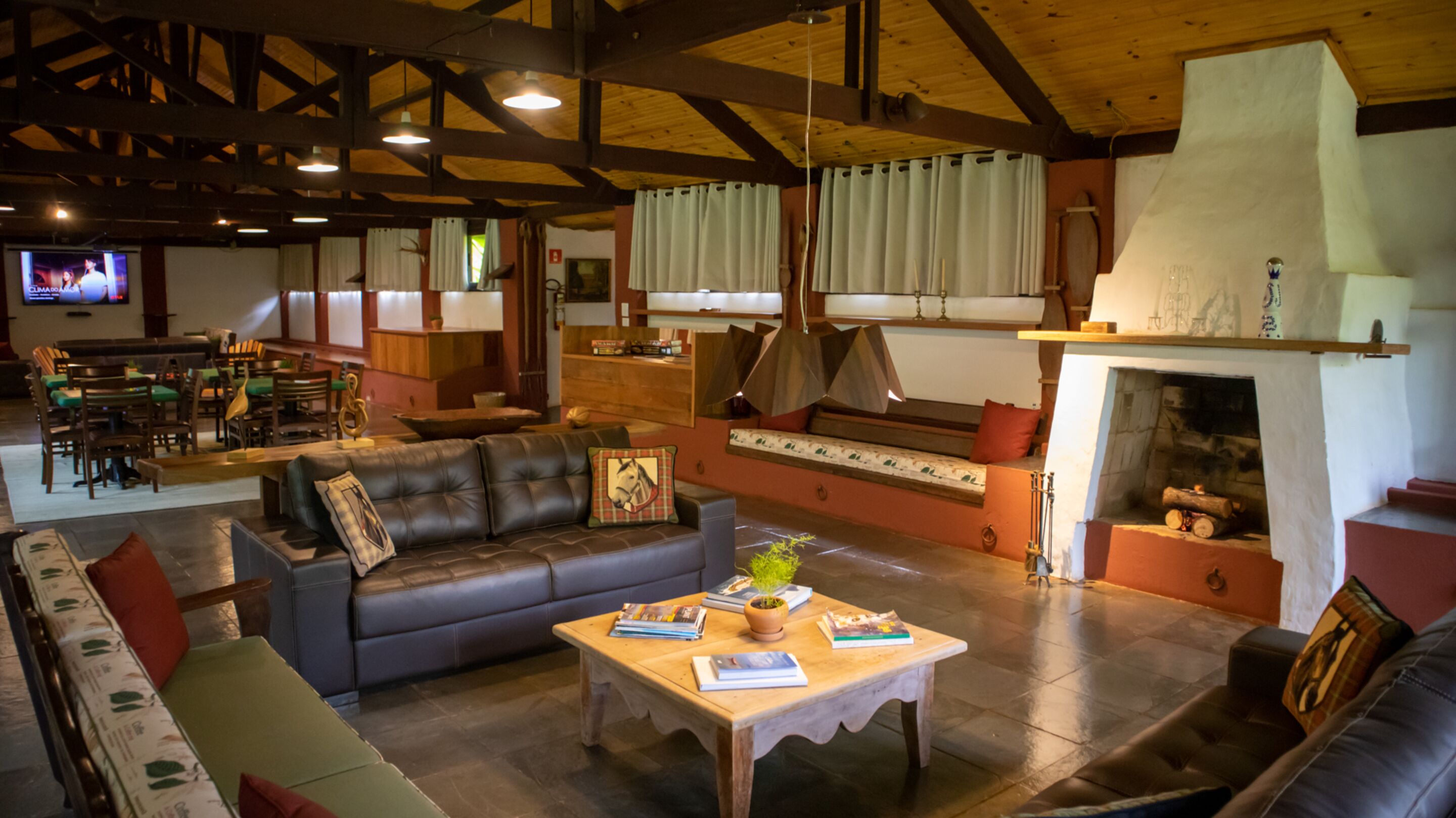 Uma sala de estar ampla com lareira, sofá, mesa de centro e área de jantar com mobiliário de madeira.