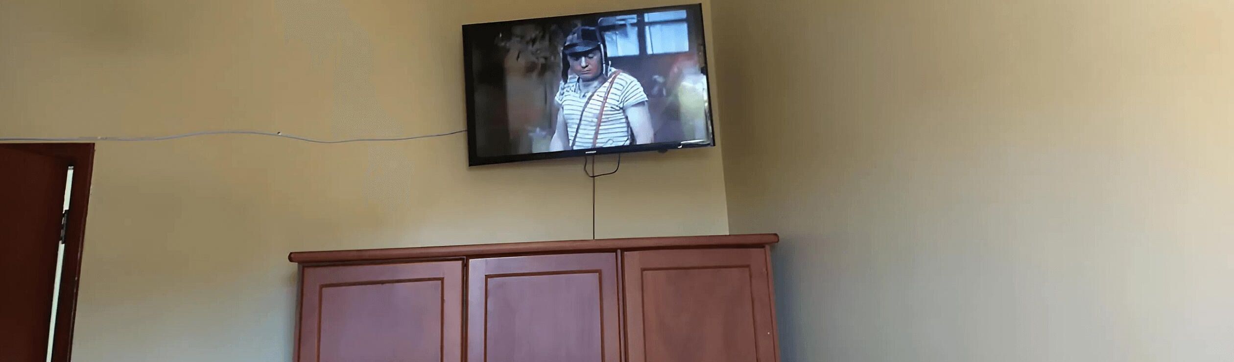 Uma televisão fixada na parede, acima de um armário de madeira.