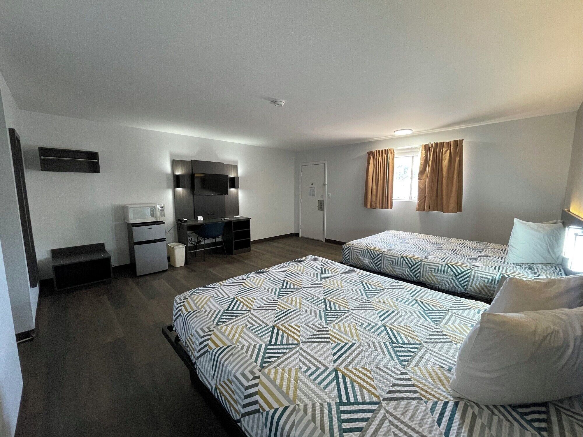 Quarto de hotel com duas camas, uma mesa, televisão e cozinha compacta.