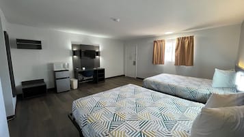 Quarto de hotel com duas camas, uma mesa, televisão e cozinha compacta.