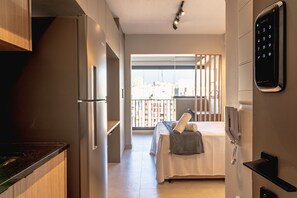 Quarto de hotel moderno com varanda, uma cama, minibar e telefone fixado na parede.