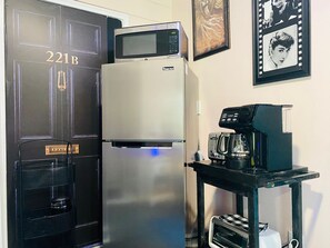Cozinha compacta com geladeira, micro-ondas, cafeteira e torradeira sobre uma mesa pequena.