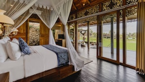 Uma cama grande com dossel, parede de pedra e vista para uma paisagem verde através de grandes portas deslizantes.