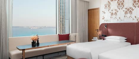 Quarto de hotel com uma janela grande, um sofá, uma escrivaninha e duas camas.
