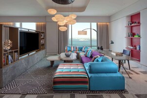 Uma sala de estar moderna com uma grande televisão de tela plana, um sofá modular, uma mesa de centro e vista para o mar.