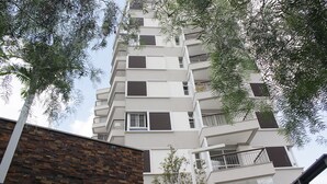 Um edifício residencial com vários andares, varandas, fachada de tijolo e árvores ao redor.