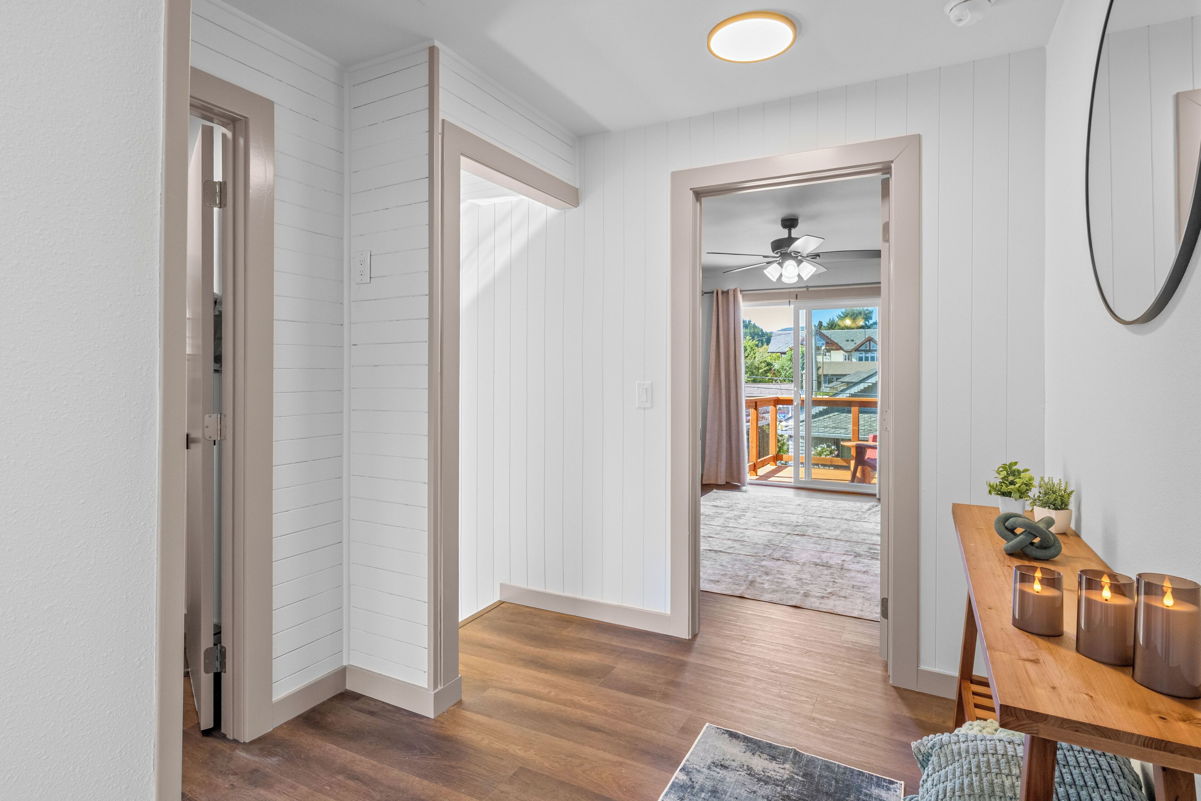 Um corredor com soalho de madeira, uma área de jantar com uma mesa e velas, e vista para uma varanda com mobiliário exterior.