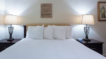Cama bem arrumada com lençóis brancos, duas mesas de cabeceira com abajures e uma placa fixada na parede.