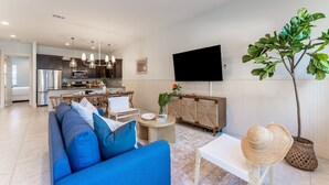 Uma sala de estar moderna com um sofá azul, uma mesa de centro e uma TV fixada na parede.