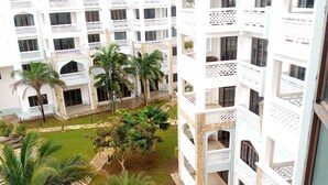 Um hotel com vários andares, varandas, um pátio com palmeiras e um caminho de pedra.