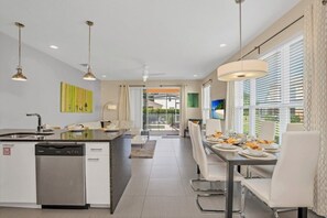 Cozinha moderna com máquina de lavar louça, área de refeições com mesa posta para quatro pessoas e vista para o exterior através de grandes janelas.