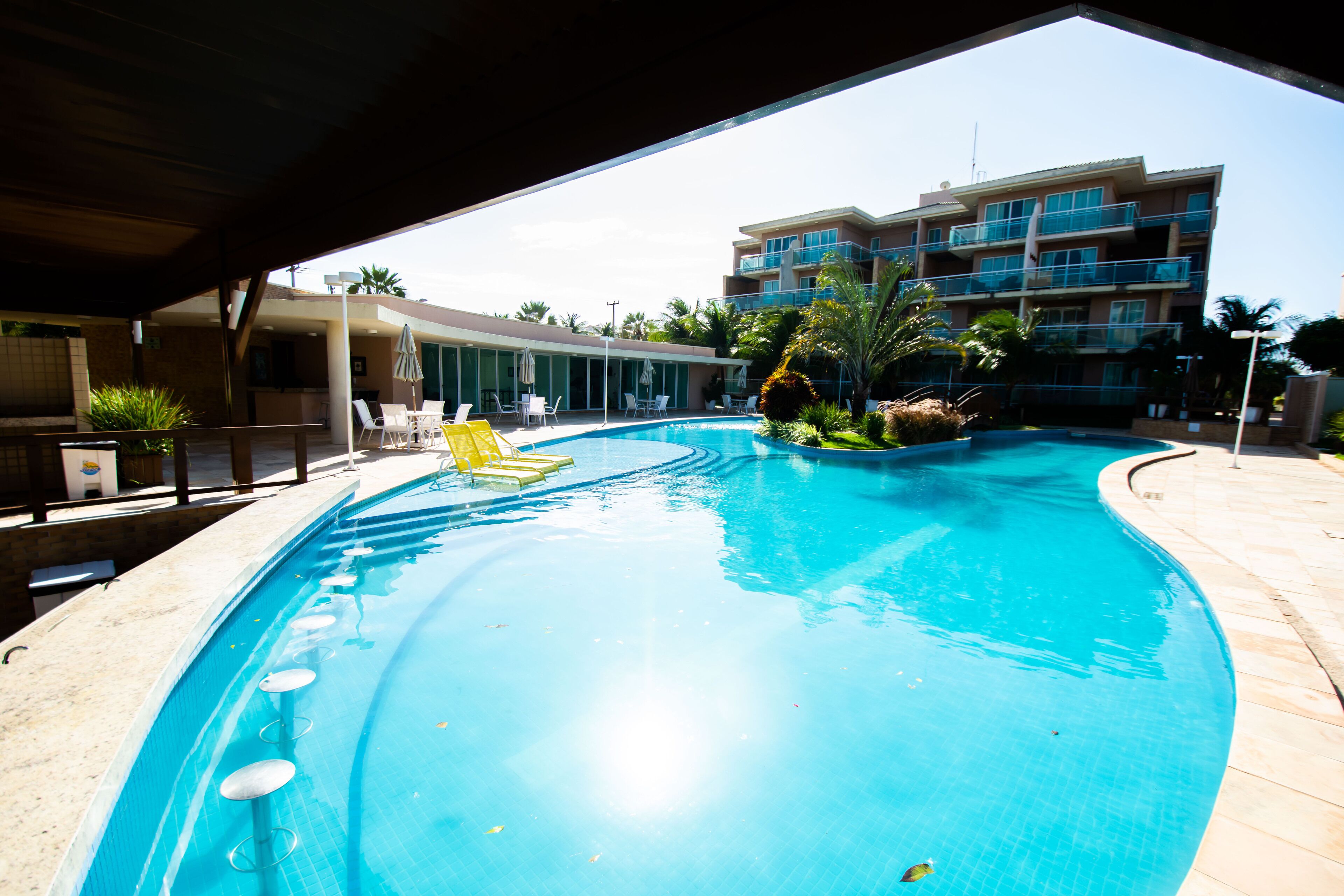 Piscina com espreguiçadeiras e um edifício ao fundo.