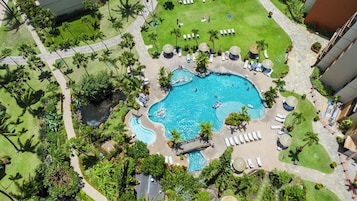 Uma piscina grande rodeada por palmeiras e espreguiçadeiras, com um caminho de pedra que leva à piscina.