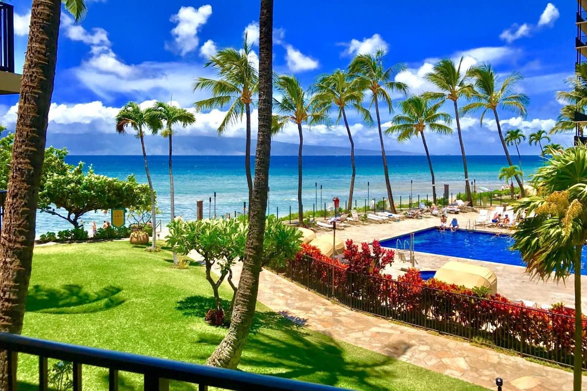 Um resort com piscina, palmeiras e vista para o oceano.