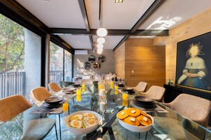 Uma área de refeições com mesa de vidro, cadeiras, itens de café da manhã e um quadro na parede.