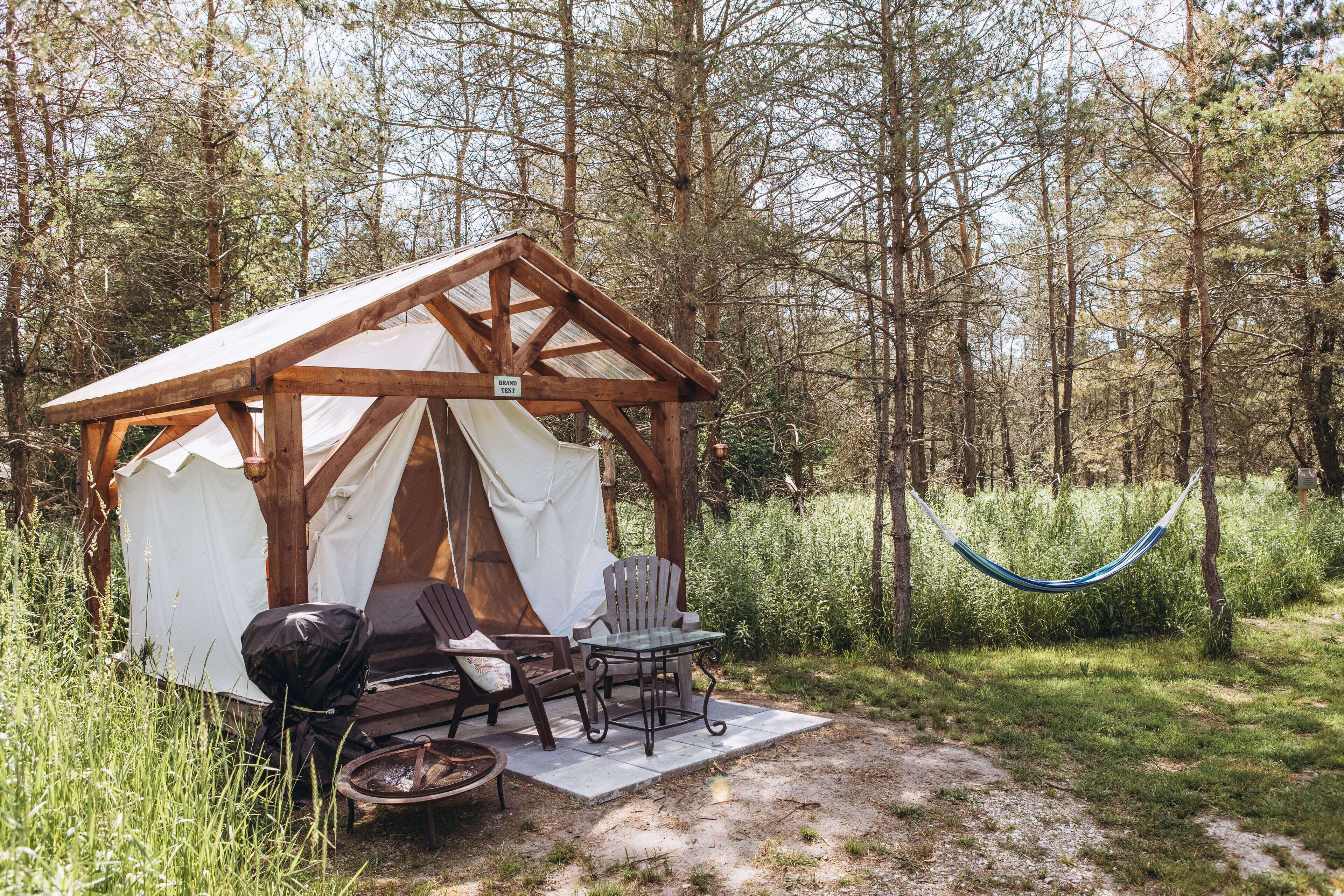Uma cabana de madeira com uma tenda, uma rede e mobiliário de exterior.