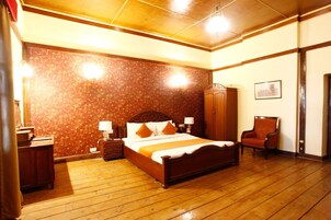 Quarto com piso de madeira, uma cama grande, mesa de cabeceira, uma cadeira e um guarda-roupa.