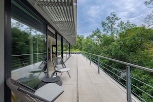 Varanda com área de estar, guarda-corpo de vidro e vista para o verde.