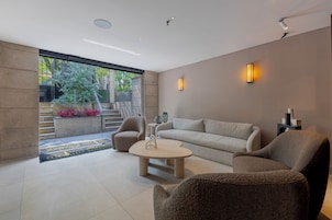 Uma sala de estar moderna com sofá, poltronas, mesa de centro e uma janela ampla com vista para o verde.