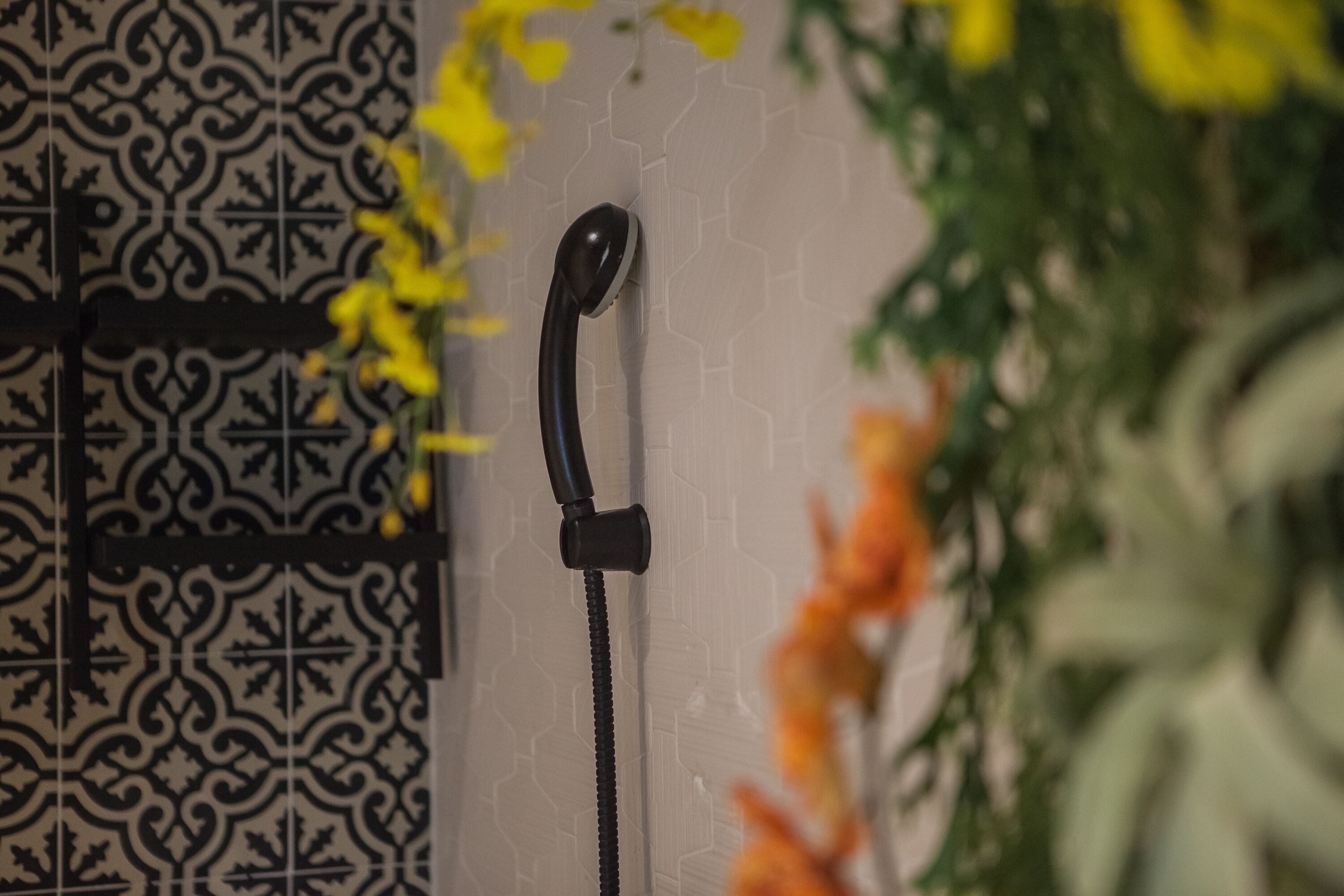 Chuveiro com mangueira preta e um bico curvo, fixado numa parede com padrão de azulejos geométricos.