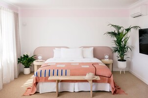 Um quarto com cama, mesas de cabeceira, um vaso de plantas e uma TV fixada na parede.