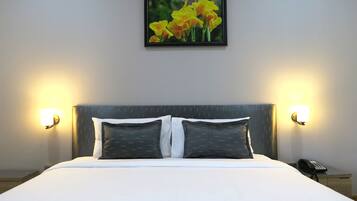 Cama bem arrumada com duas almofadas, um quadro com flores na parede e luminárias de cabeceira.