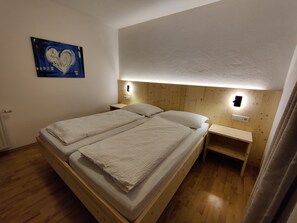 Cama de casal com duas almofadas, mesa de cabeceira, luminária na parede e um quadro.