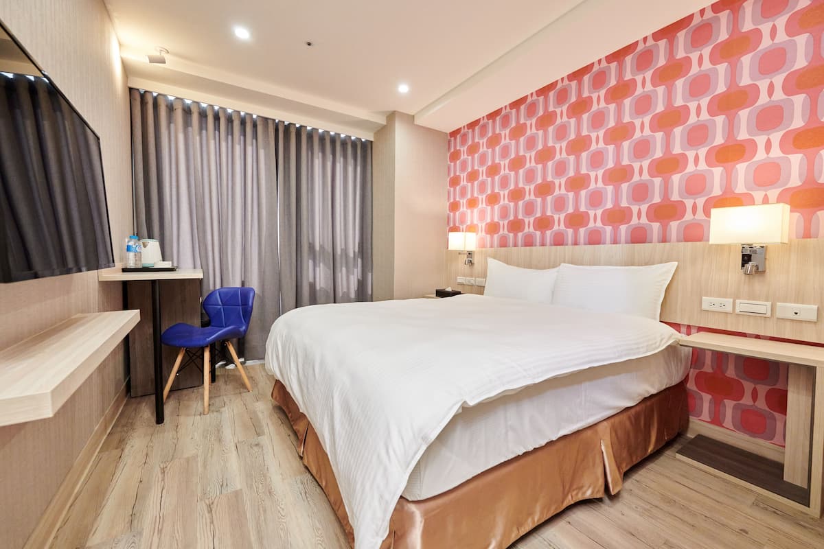 Quarto de hotel com uma cama grande, uma escrivaninha, uma cadeira e uma parede com padrão geométrico.